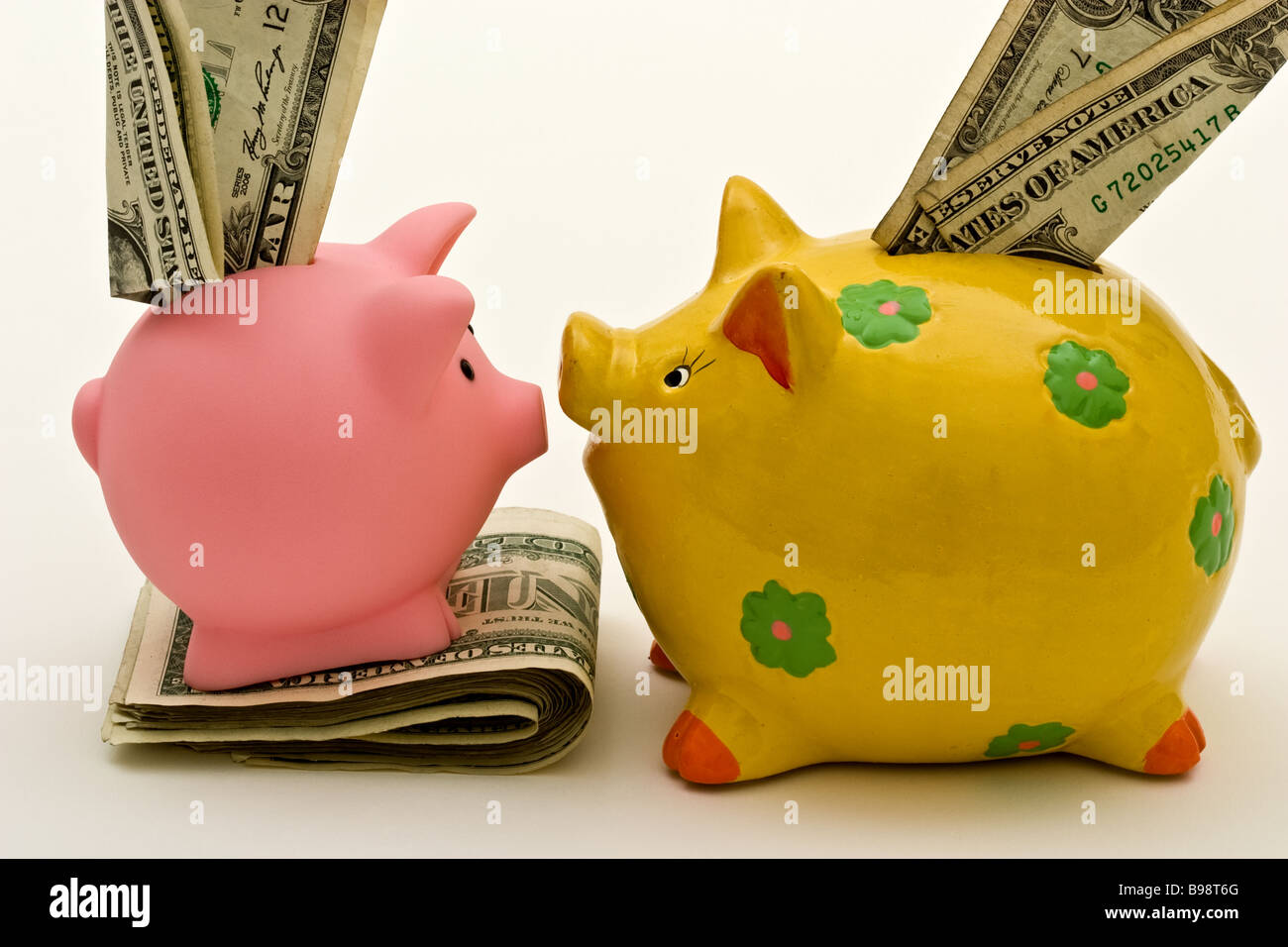 Two piggy banks, with American dollar bills in their coin slots, and ...