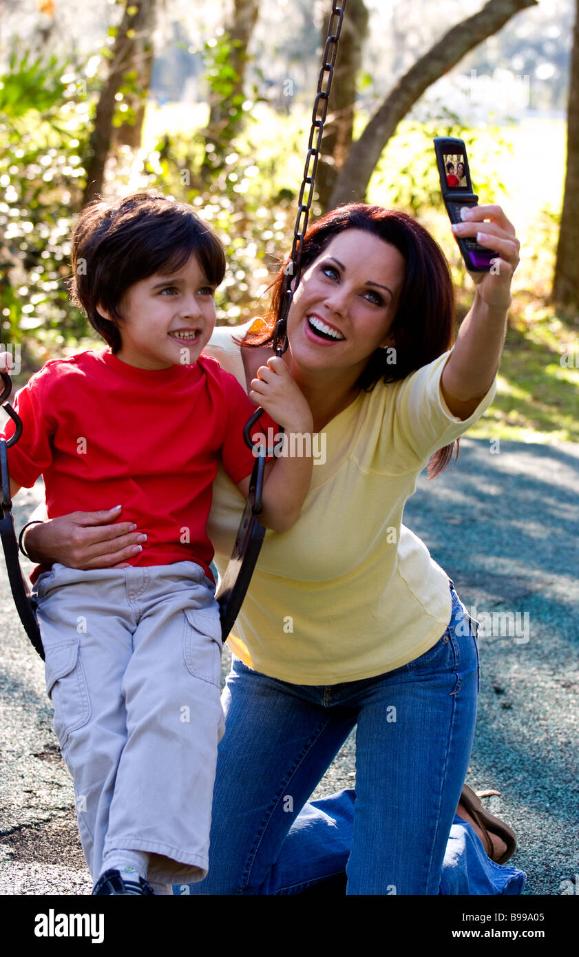 Hispanic Mother And Son Having Fun Outdoors In Park On Swing Taking Cell Phone Picture And