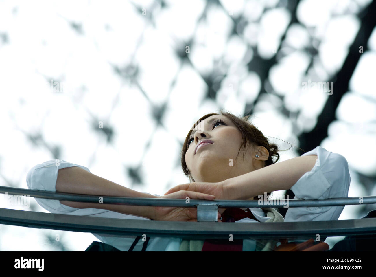 Young woman leaning against railing with arms folded, low angle view ...