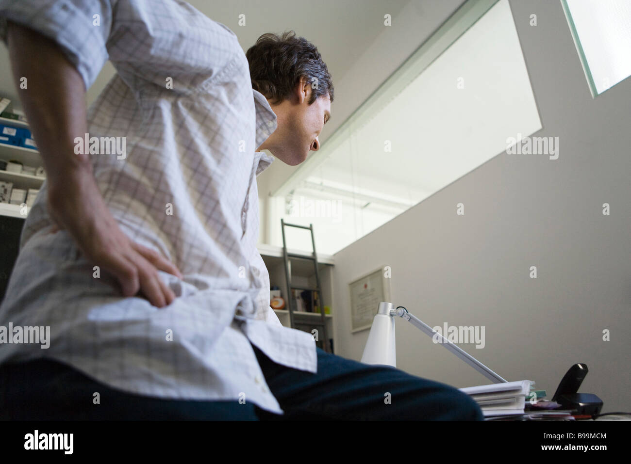 Man sitting on desk, looking away, low angle view Stock Photo - Alamy