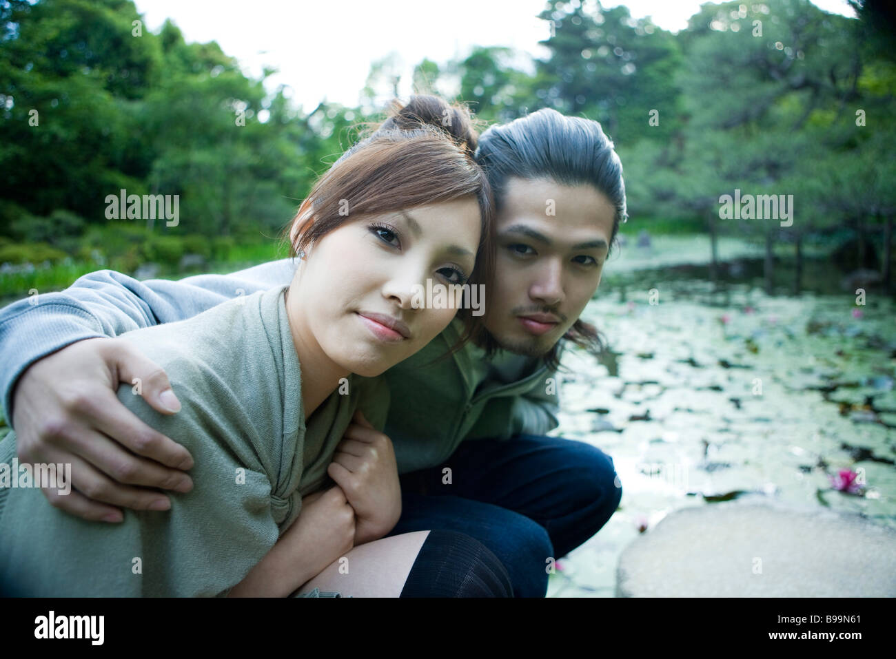 Young couple crouching beside pond, portrait Stock Photo - Alamy