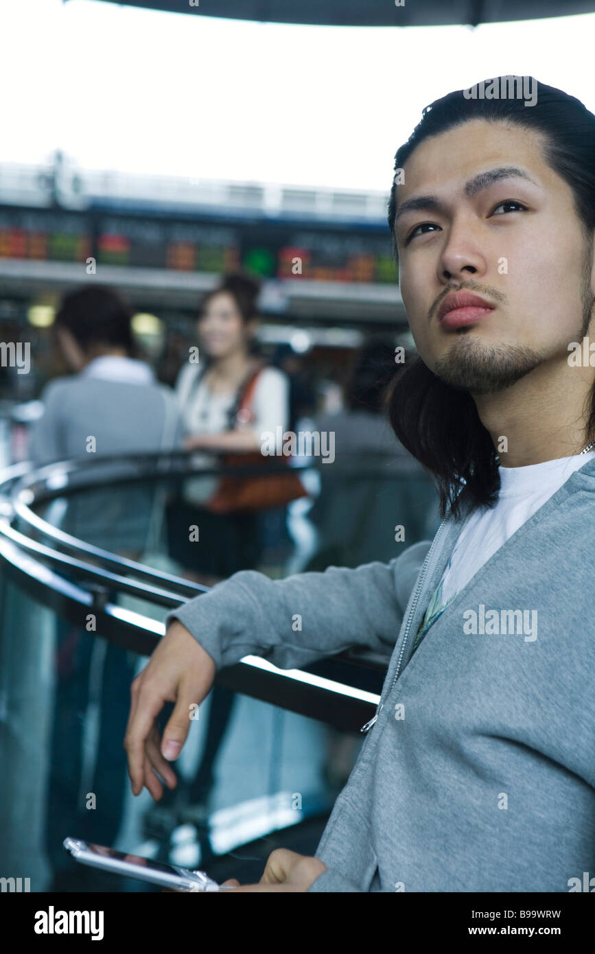 Young man leaning against railing, holding cell phone Stock Photo - Alamy