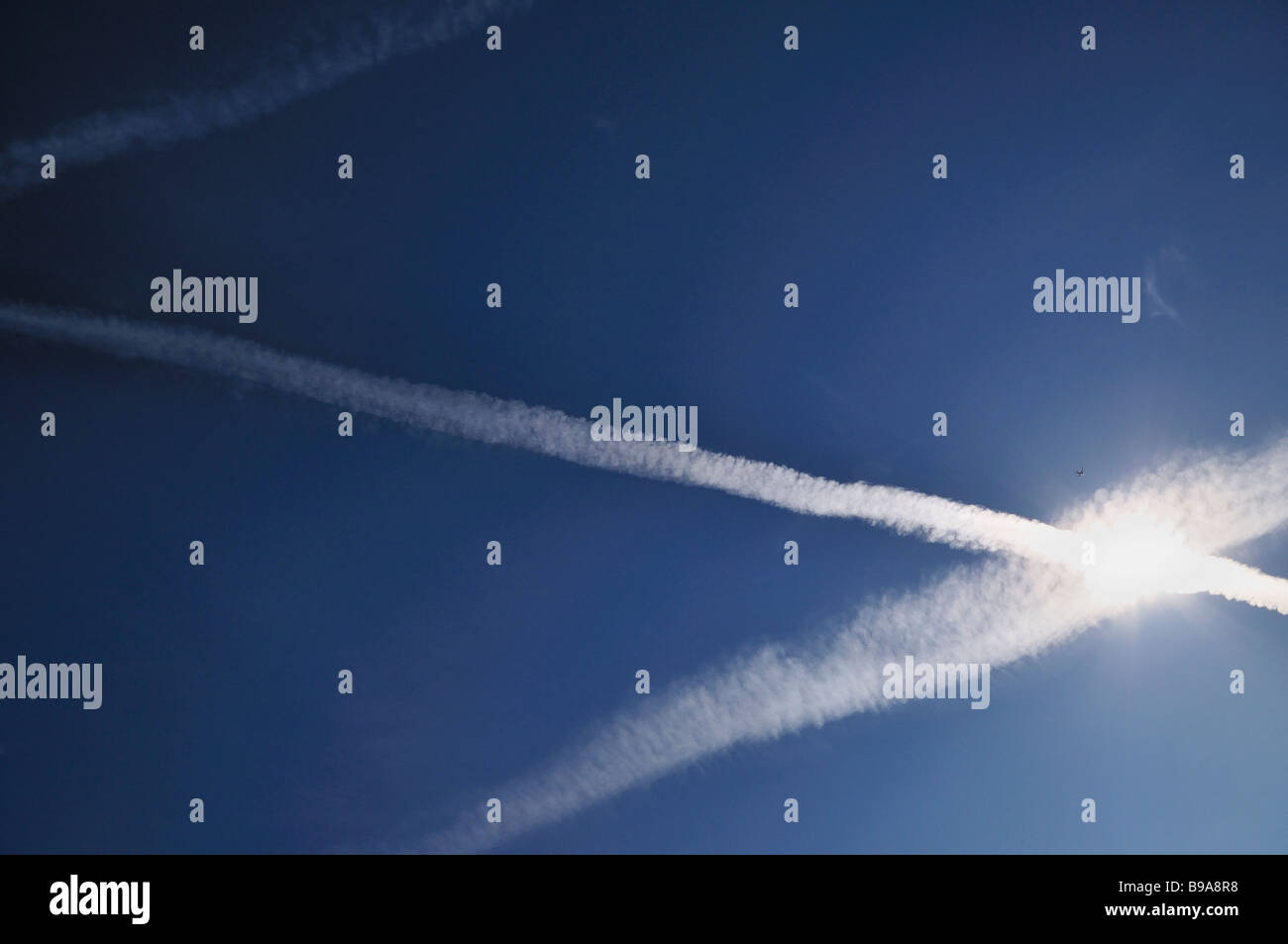 A jet flies into the sun in a sky full of crossing contrails Stock ...