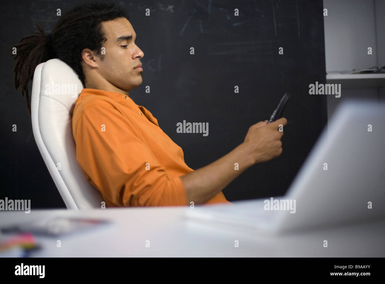 Man sitting in chair, looking down at cell phone Stock Photo - Alamy