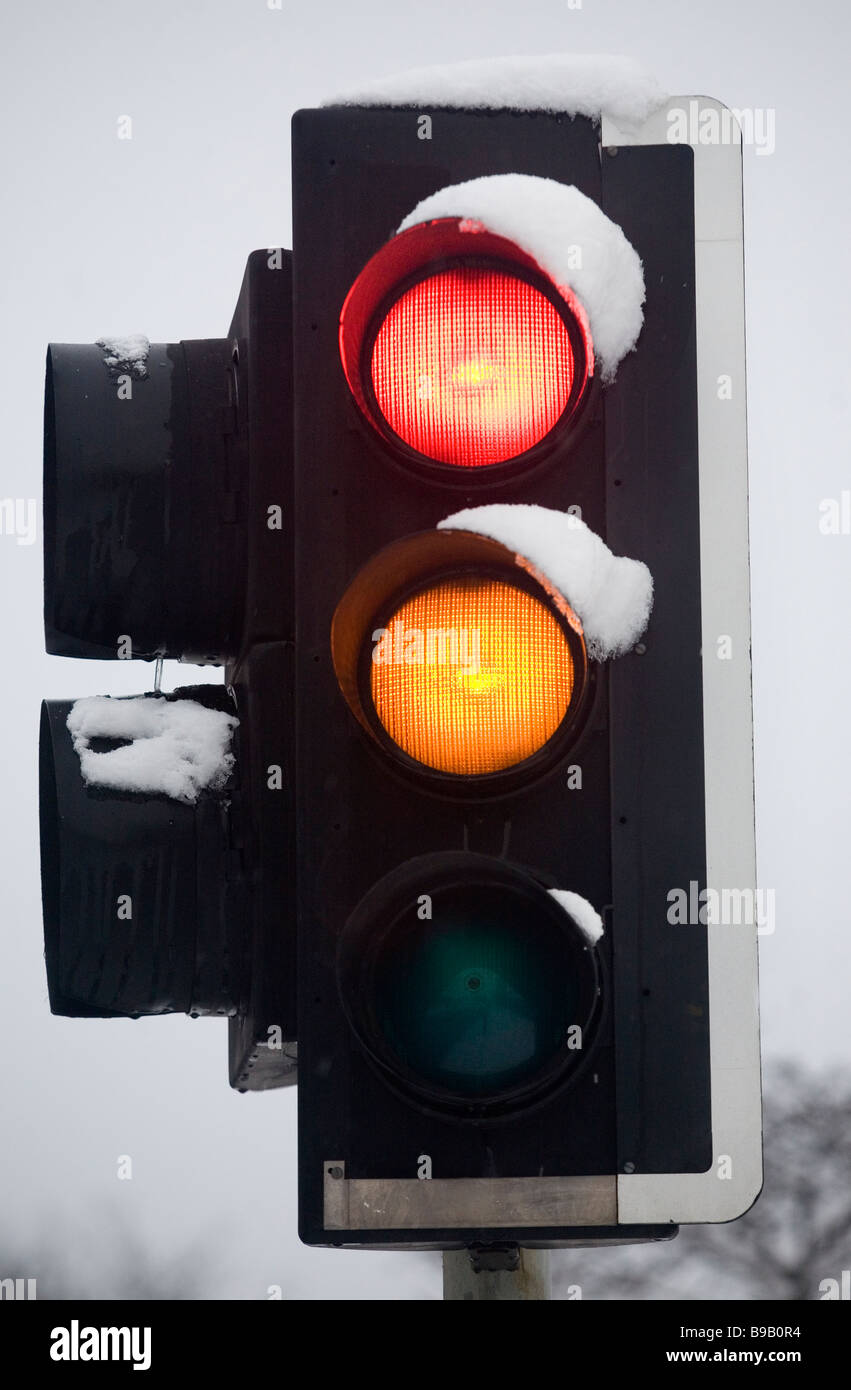 A British traffic light changes from red to amber as snow settles on it ...