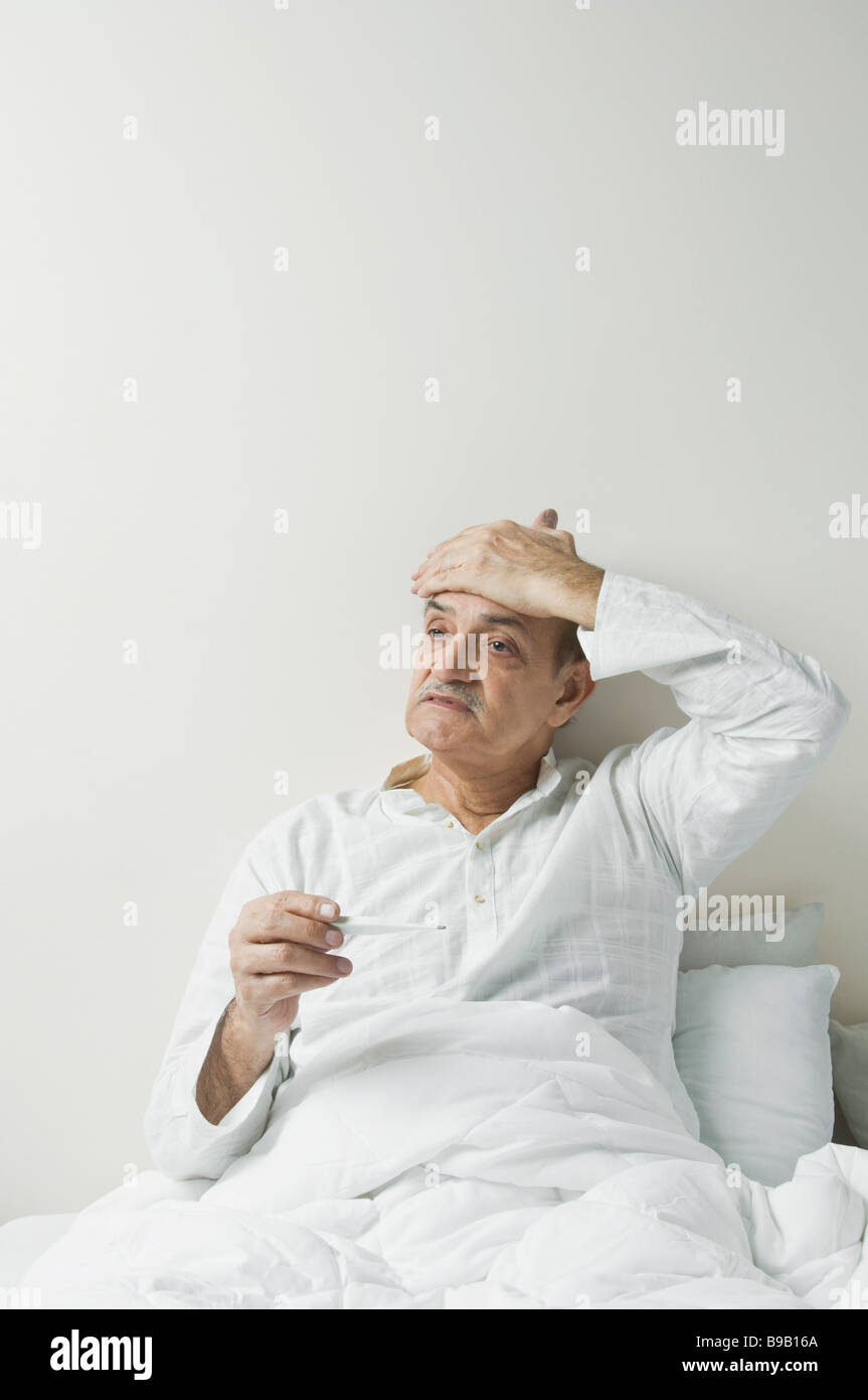 Man sitting on the bed and checking his temperature Stock Photo - Alamy