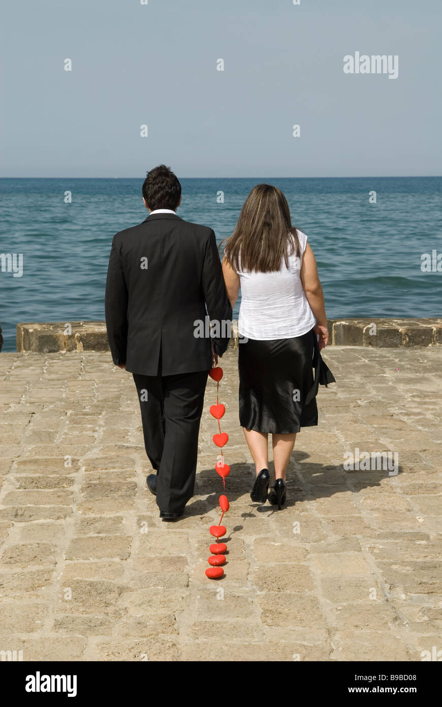 Man and woman walking towards the sea and dragging a chain of red ...