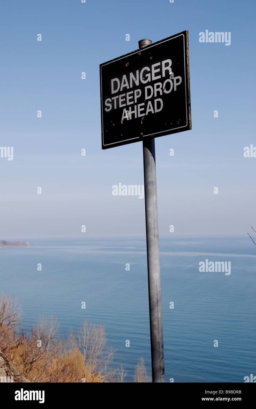 A danger sign warning of a steep drop ahead on the edge of a cliff ...