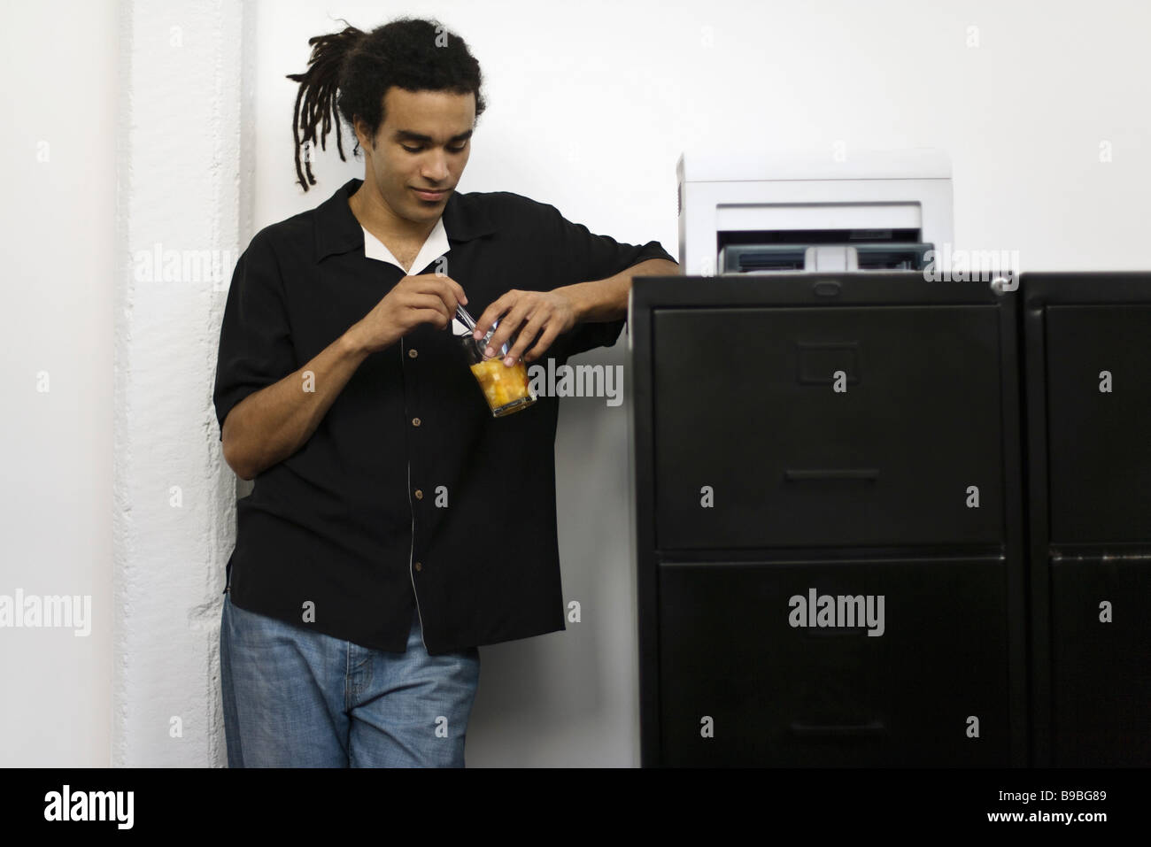 Man leaning against filing cabinet, stirring drink Stock Photo - Alamy
