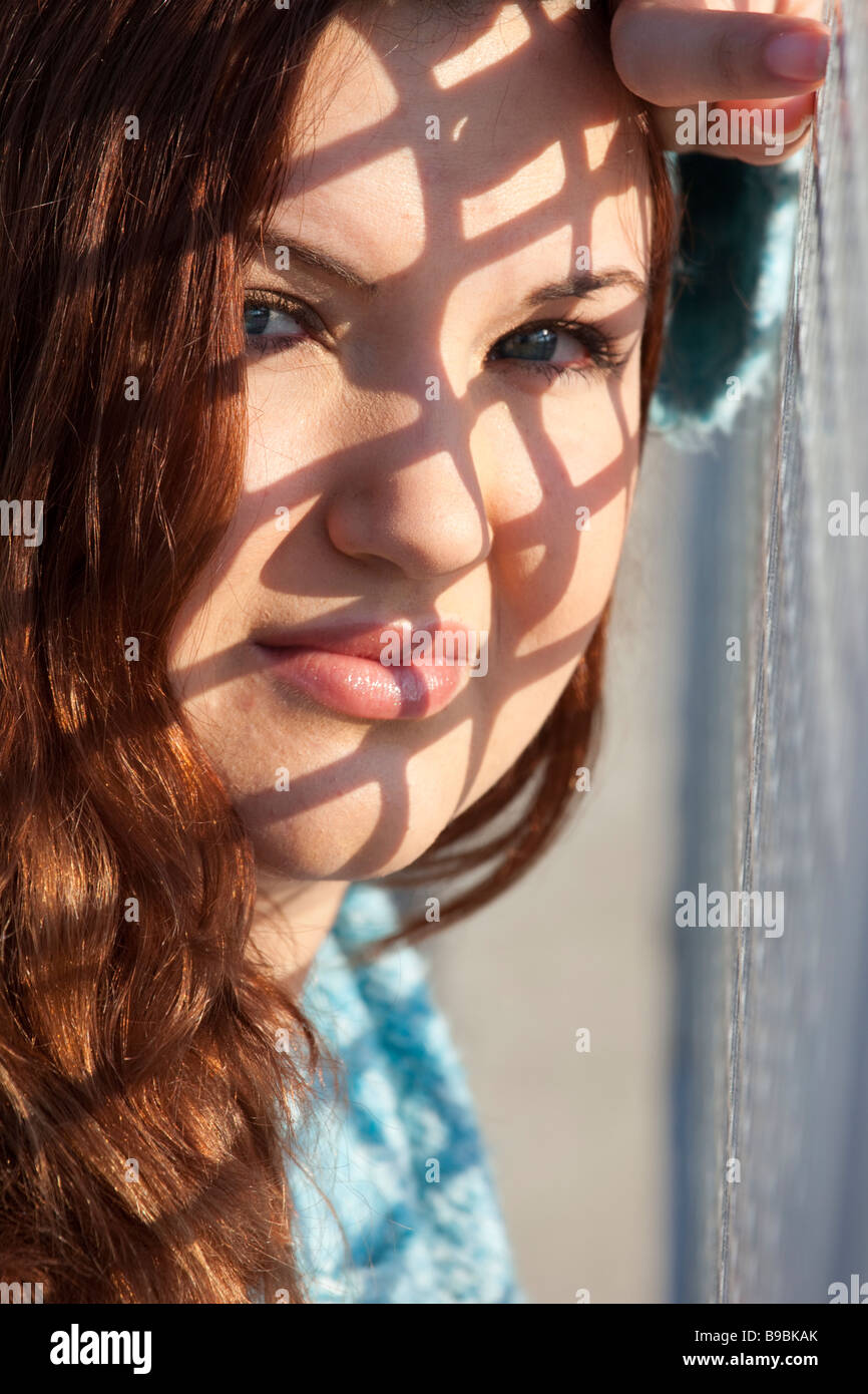 A woman leaning against a checkered fence with morning sunlight ...
