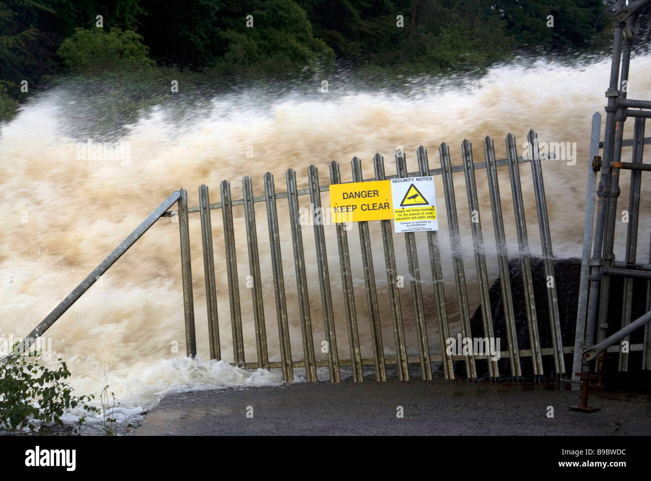 Water rushing out the bottom of a dam, behind a metal fence with ...