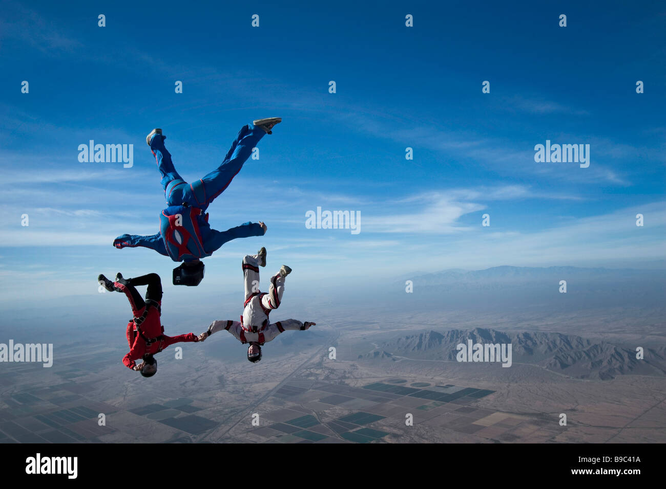 Three skydivers freefalling head first with mountains in the background ...