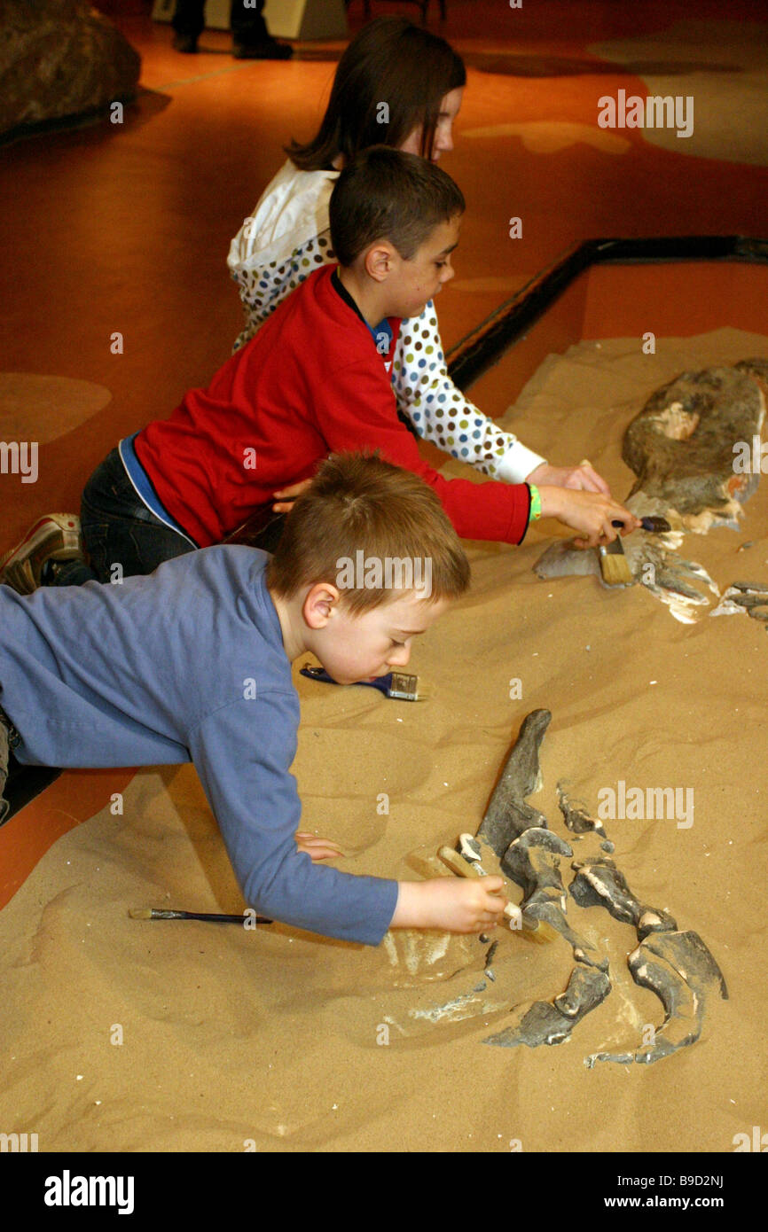 Young children learning about archaeology by un covering dinosaur bones ...