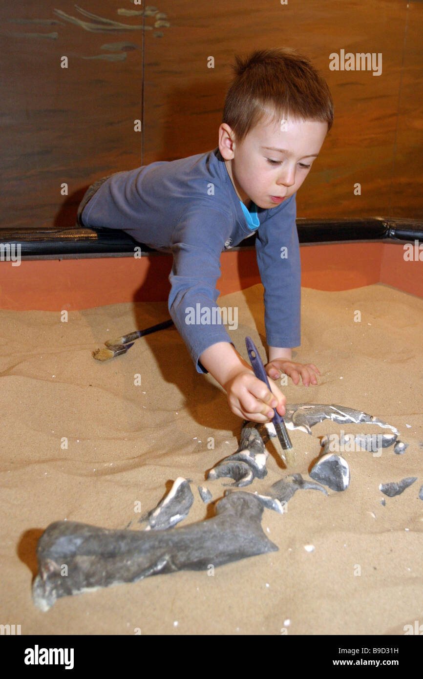 Young children learning about archaeology by un covering dinosaur bones ...