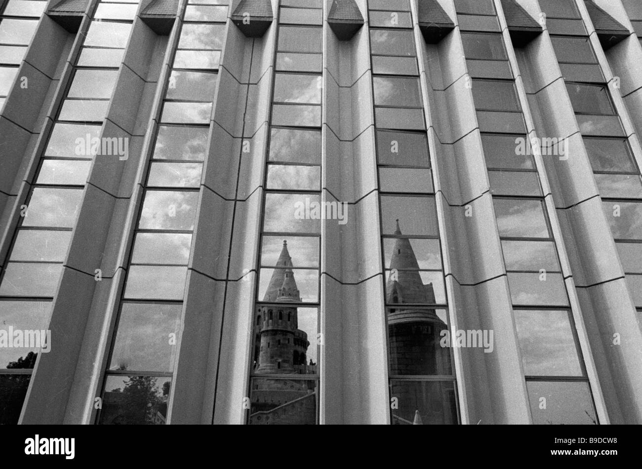 Gothic towers reflected in the windows of a glass and concrete building ...