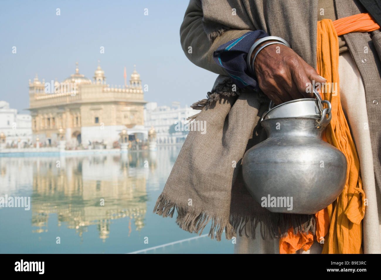 Man holding a kamandal with a temple in the background, Golden Temple ...