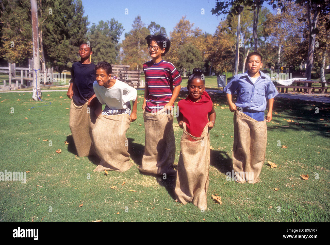Racial mix kid boy girl play jump sack race park picnic compete chase ...