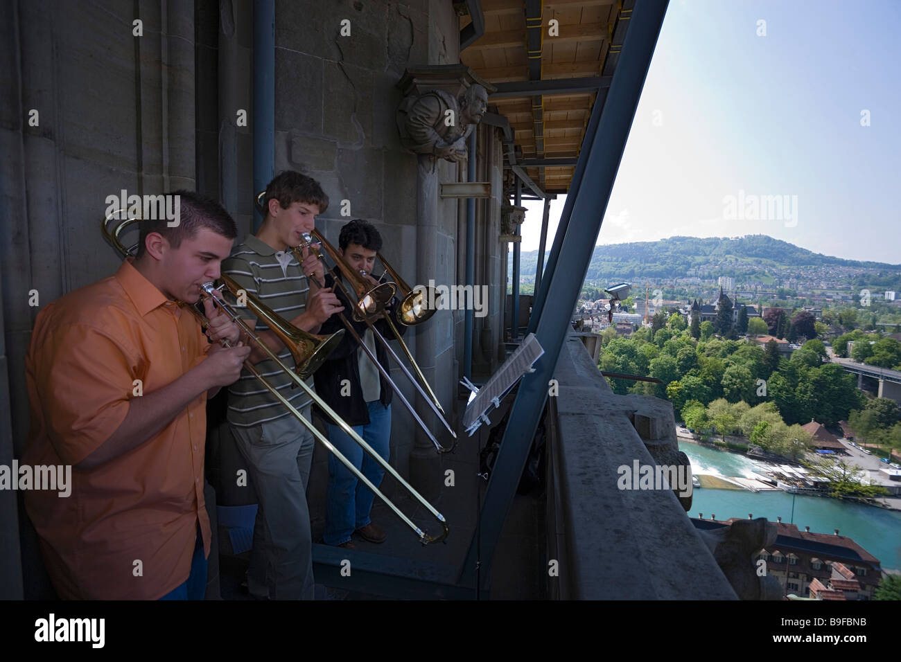 Three young men playing trombones on balcony of the Münster of Berne ...