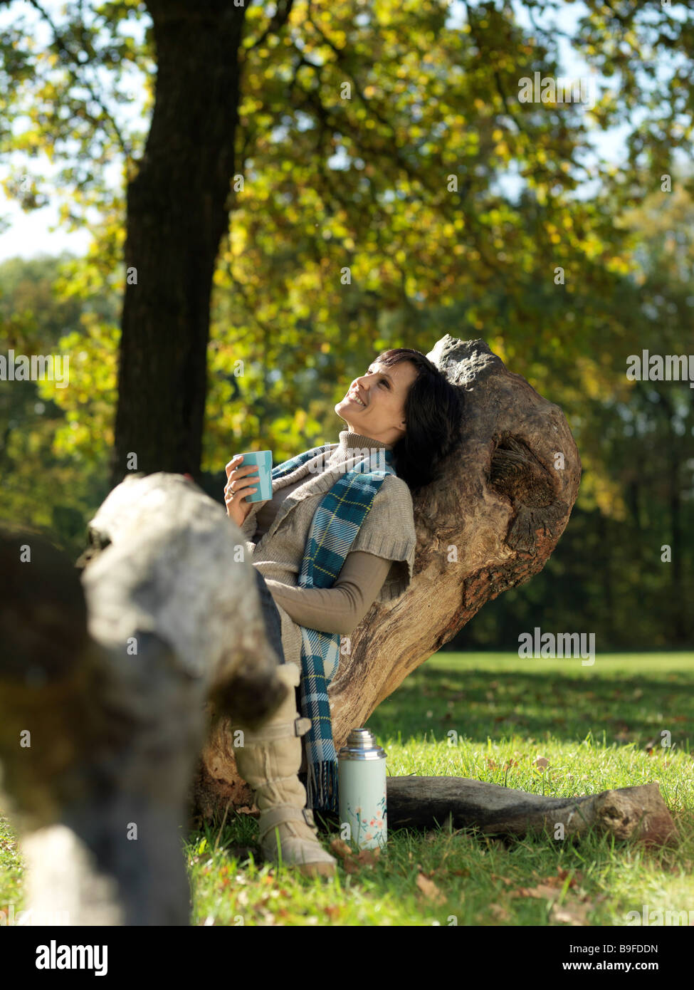 Mature woman sitting on fallen tree and smiling Stock Photo - Alamy