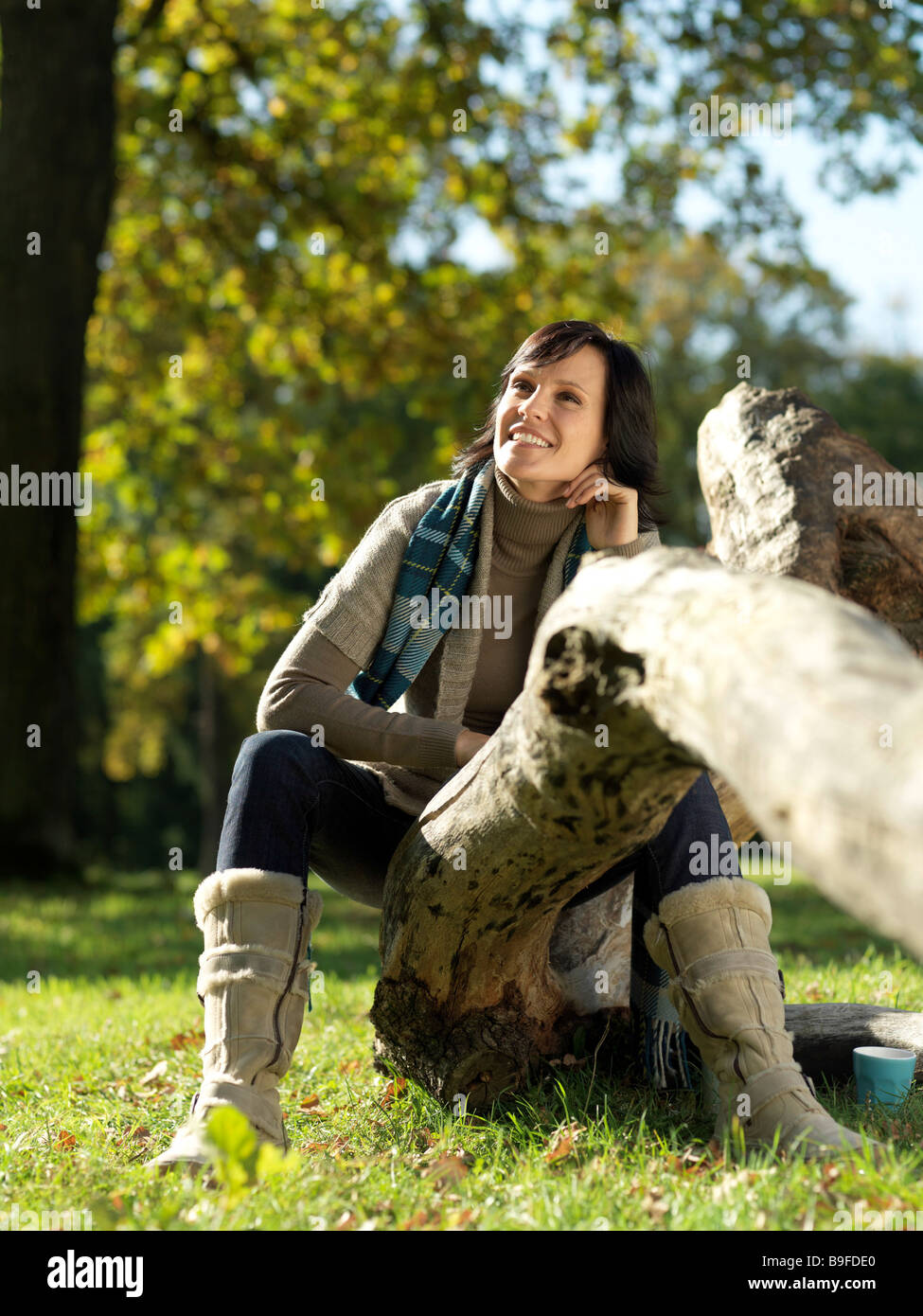 Mature woman sitting on fallen tree and smiling Stock Photo - Alamy