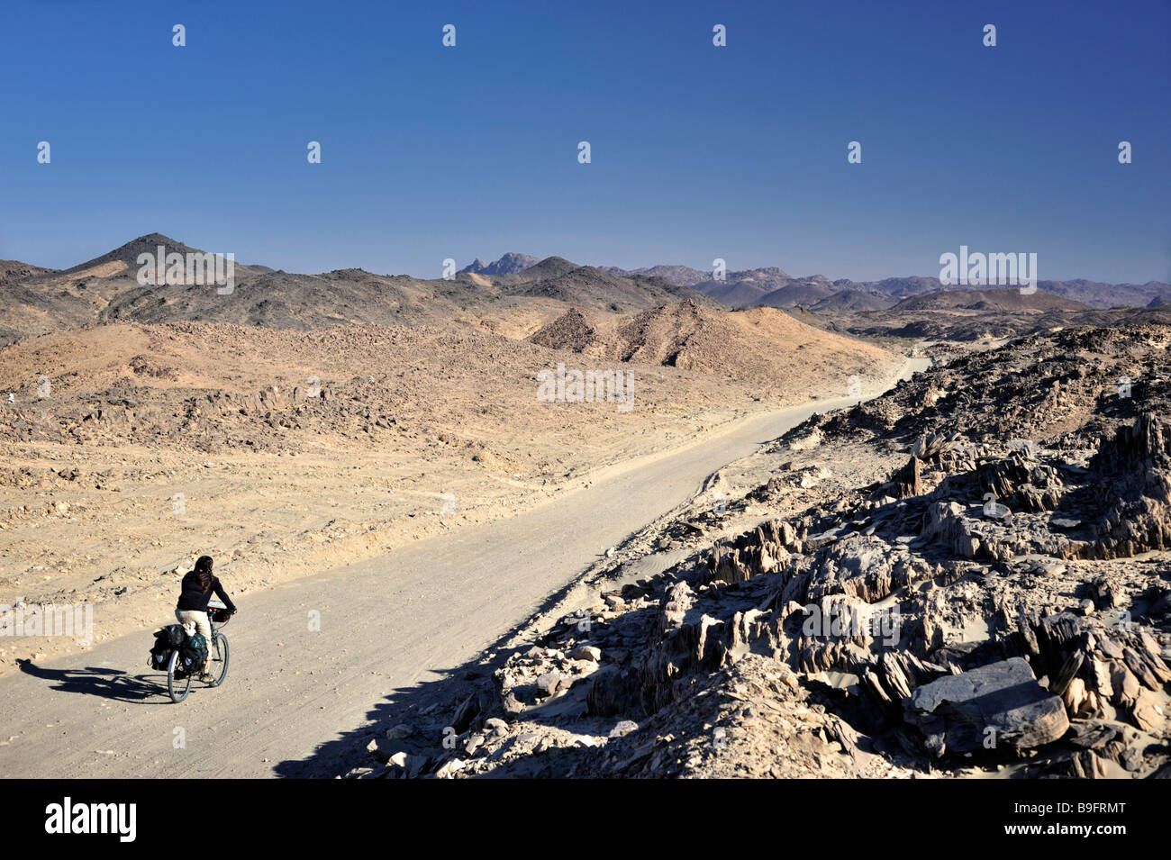 Female western touring cyclist with fully loaded bicycle on rough road ...