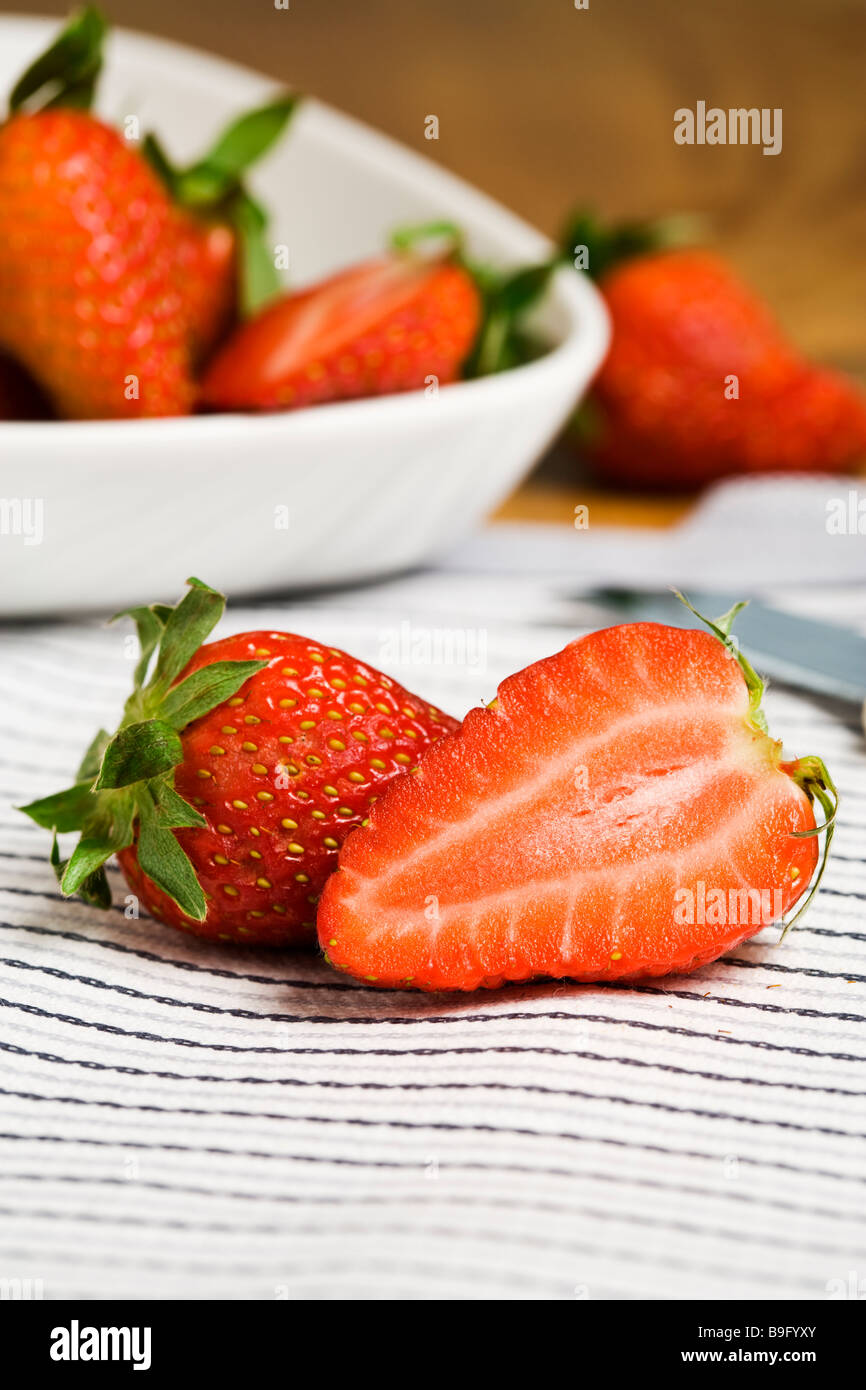 a whole and a halved strawberry lying on kitchen towel. knife and bowl ...