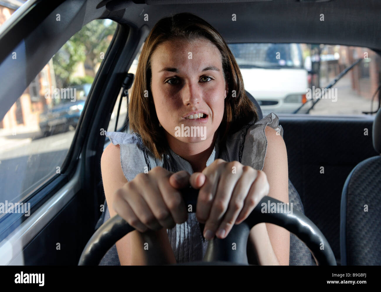 A nervous female learner driver sits gripping the steering wheel of a ...