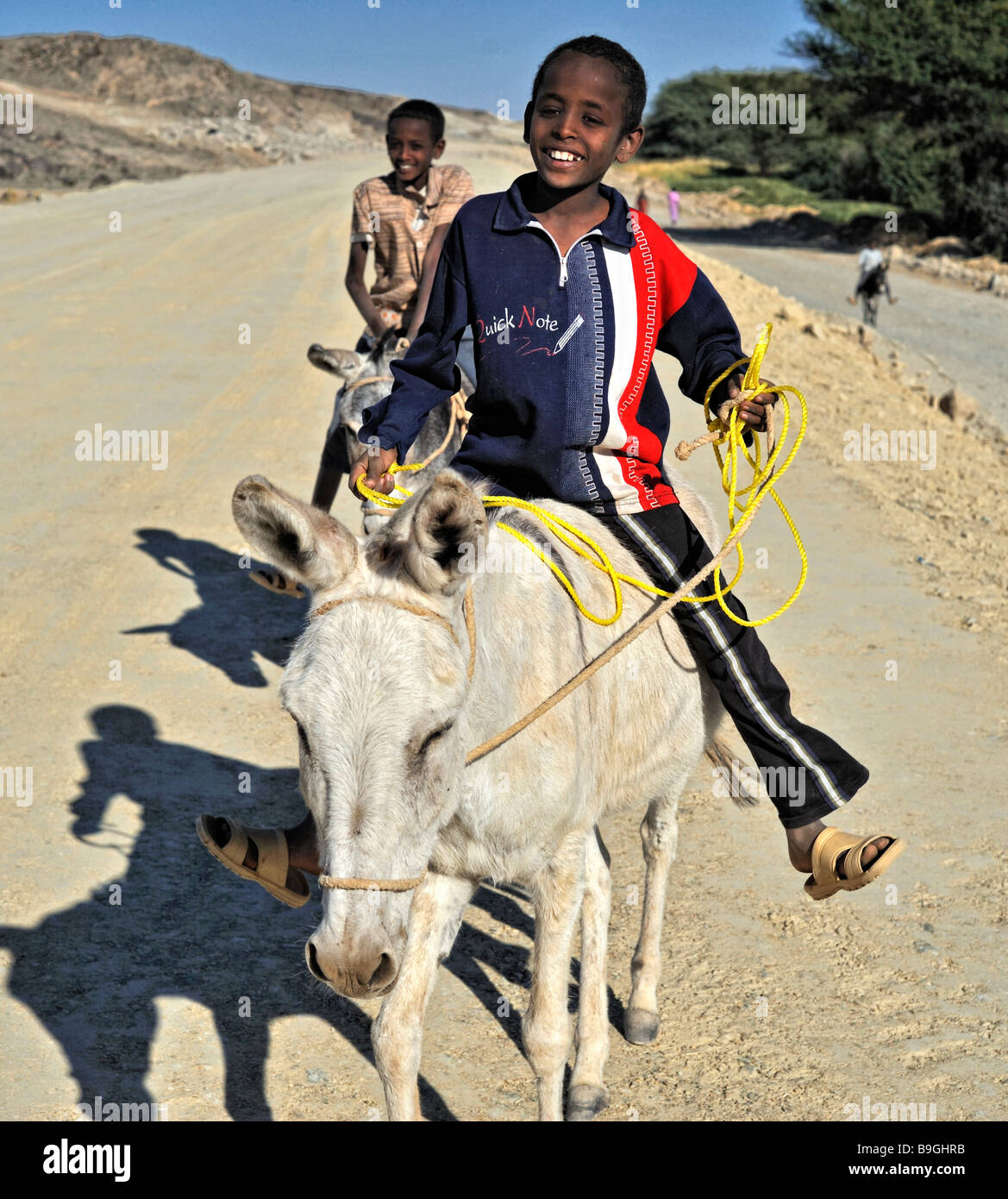 Two boys on donkeus. Smiling and showing teeth. On dusty unmade raod in ...