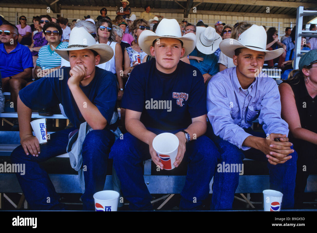 Three young cowboys sit in the grandstand watching the rodeo at the Mid ...