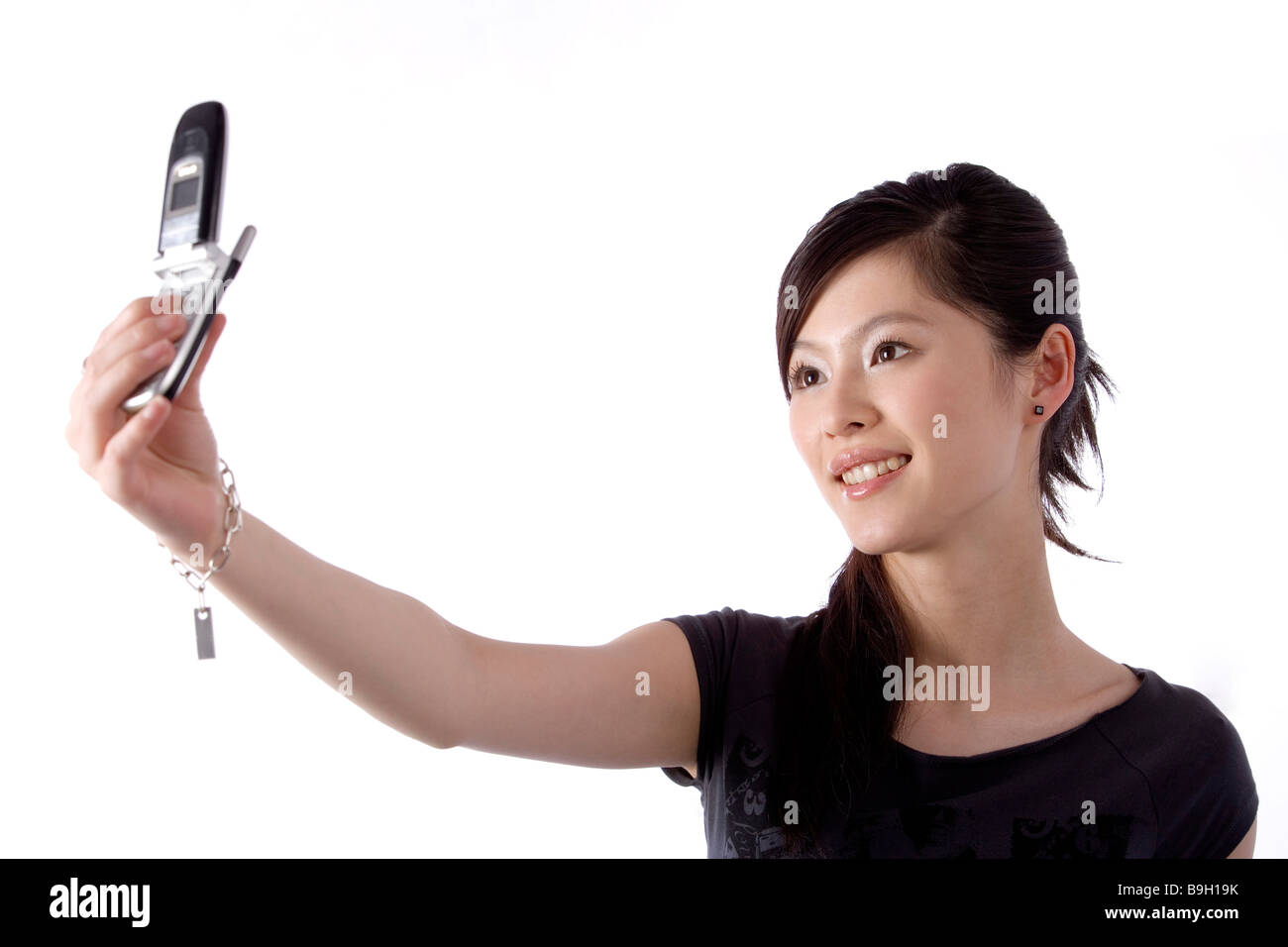 One young woman photographing herself with mobile phone against white ...
