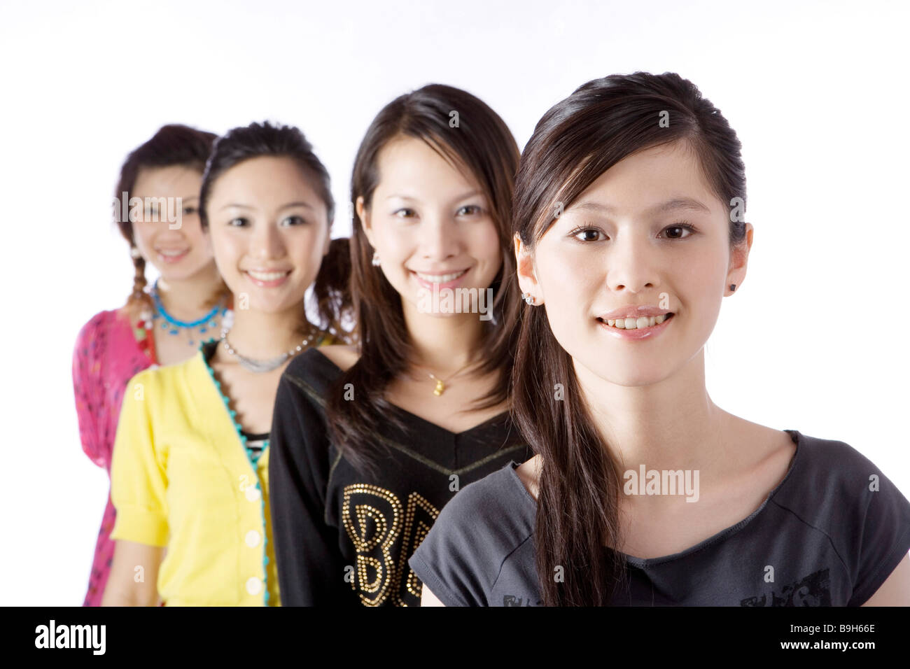 Four young women standing in a row smiling portrait Stock Photo - Alamy