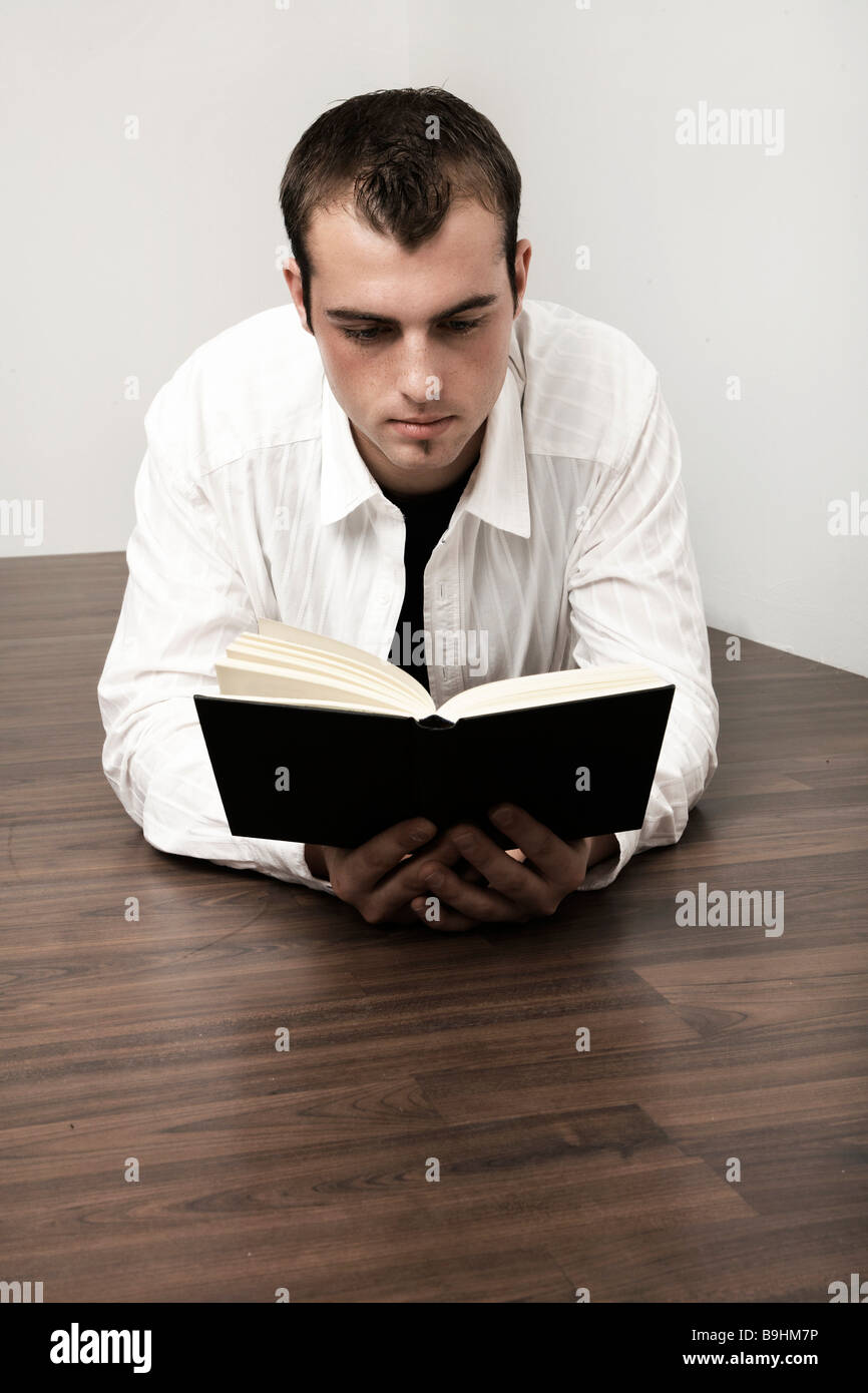 Young man lying on the floor, reading a book intently Stock Photo - Alamy