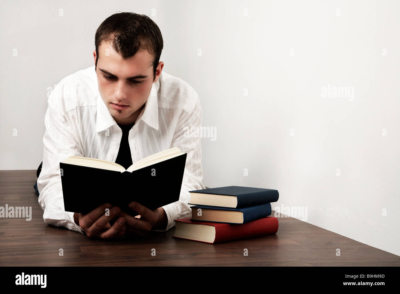 Young man lying on the floor, reading a book intently Stock Photo - Alamy
