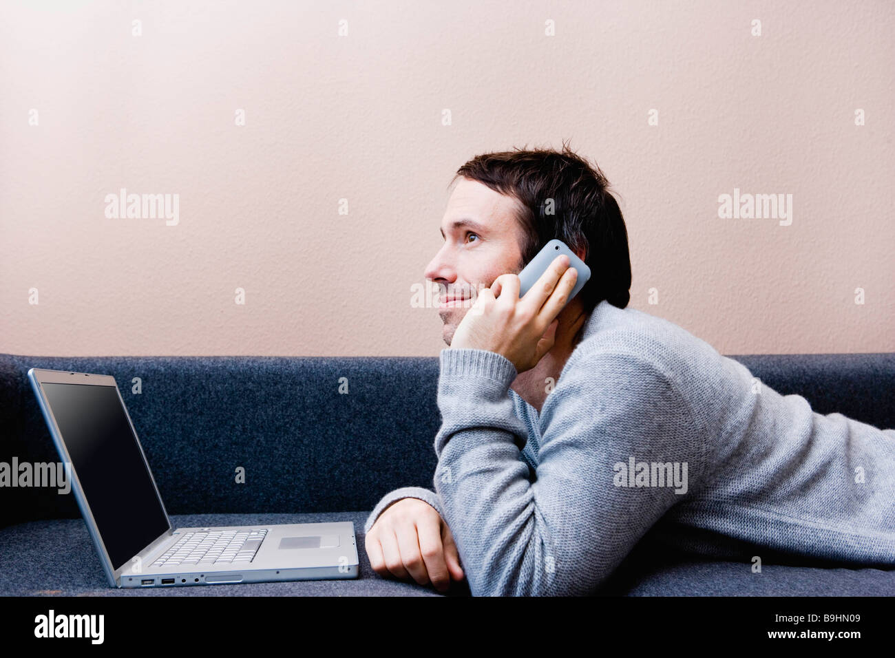 Man laying with laptop on couch Stock Photo - Alamy
