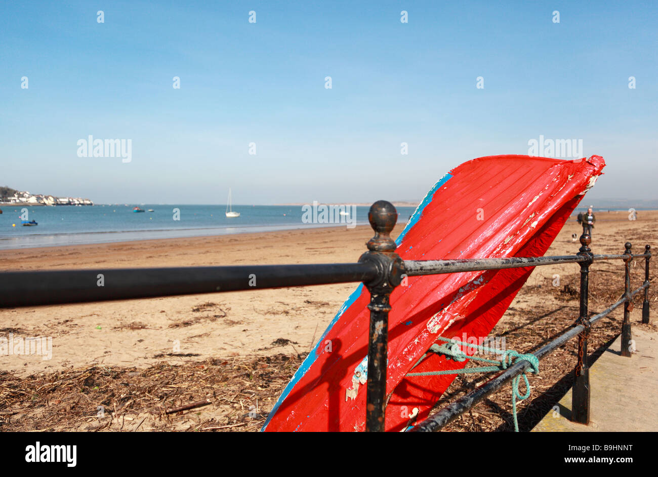 A bright red dinghy leaning against railings alongside a beach Stock ...
