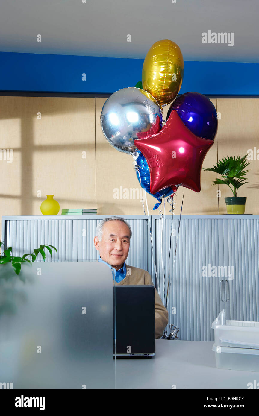 Senior man with balloons at office desk Stock Photo - Alamy