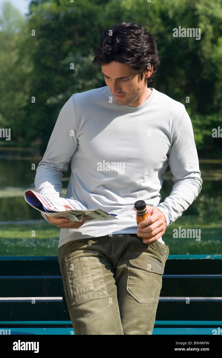 Man reading while leaning against a park bench Stock Photo - Alamy