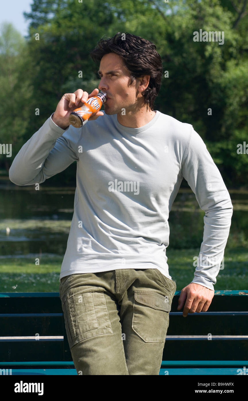 Man drinking while leaning against a park bench Stock Photo - Alamy