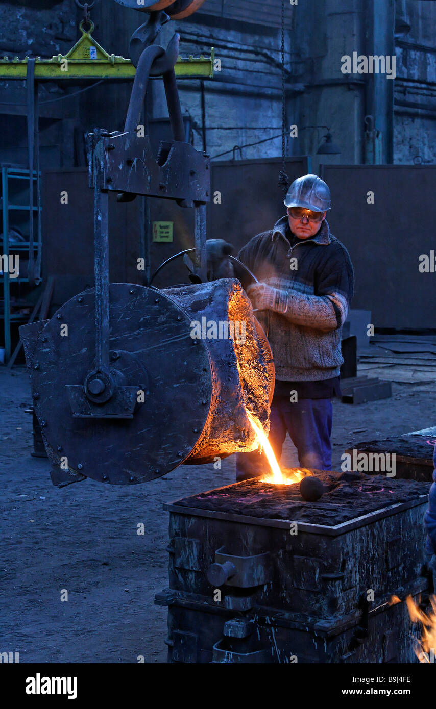 Founder tipping small crane ladle with molten iron into molds ...