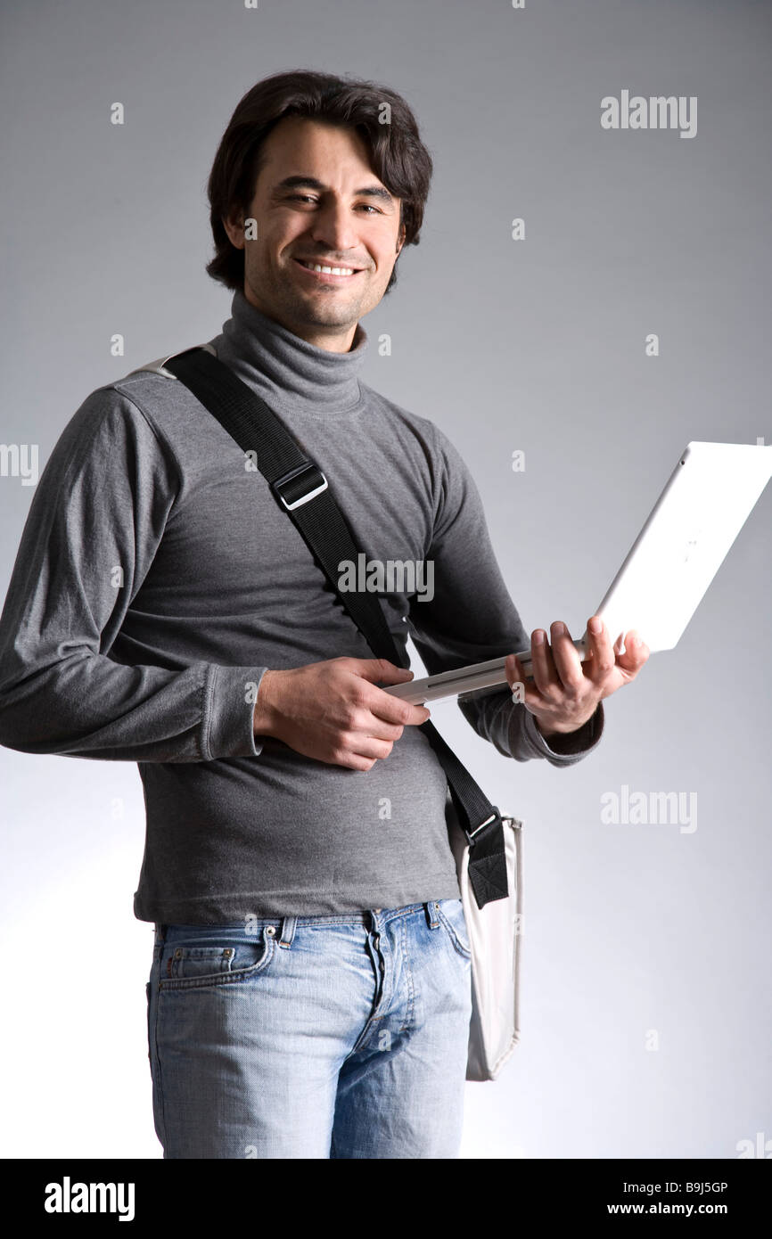 Young man with a bag, holding a laptop Stock Photo - Alamy