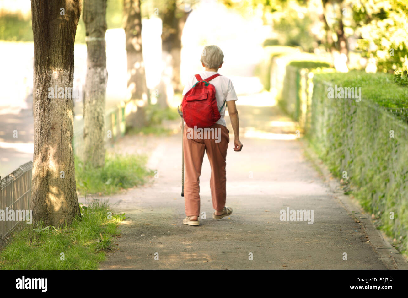 elderly woman walking in a green park with a red back pack on her ...