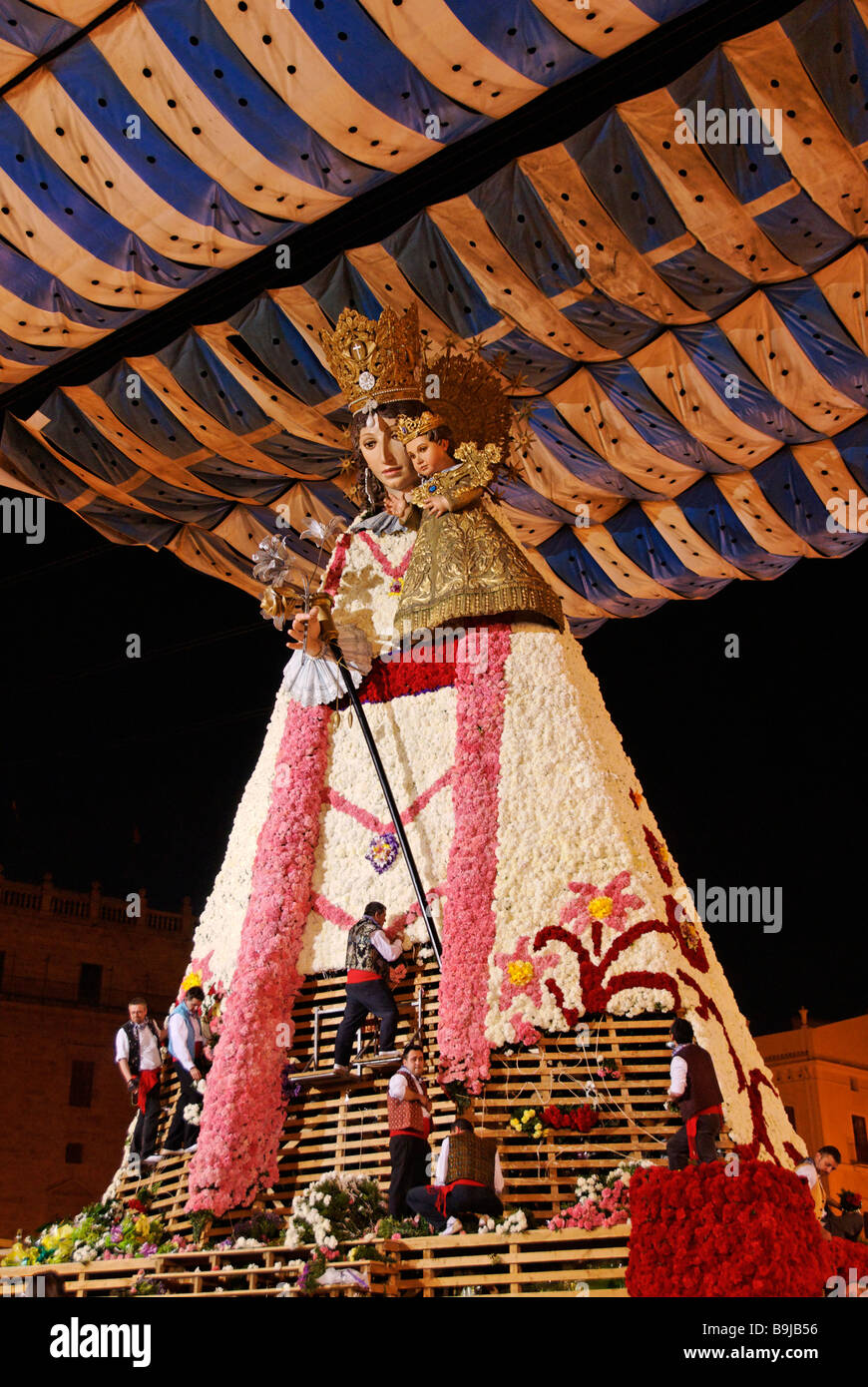 Men placing flower offerings on large wooden replica statue of Virgen ...