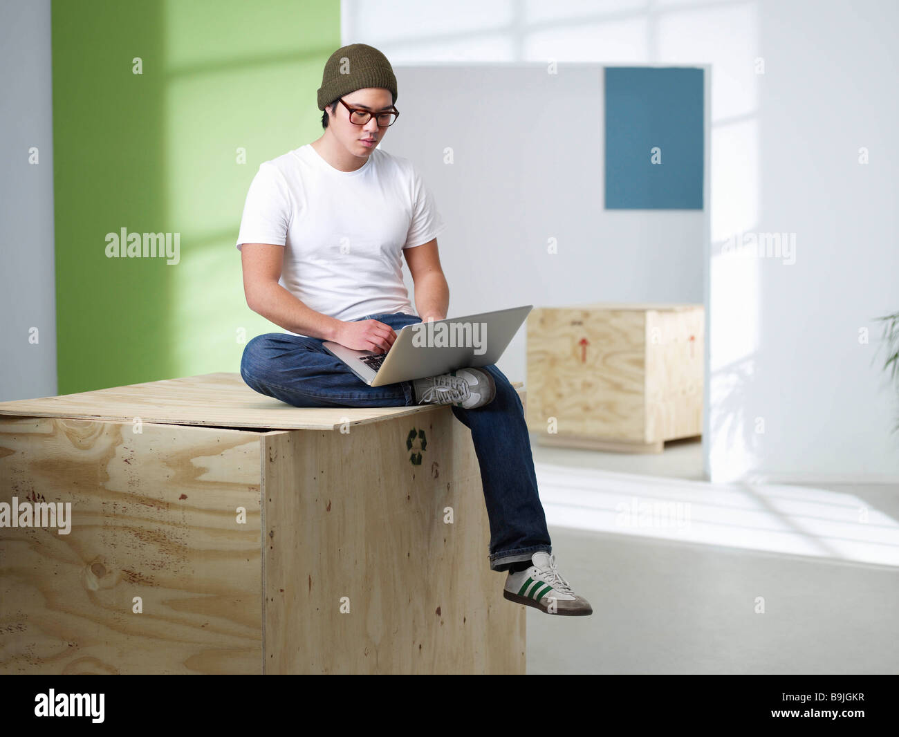 Young man sitting on box with laptop Stock Photo - Alamy