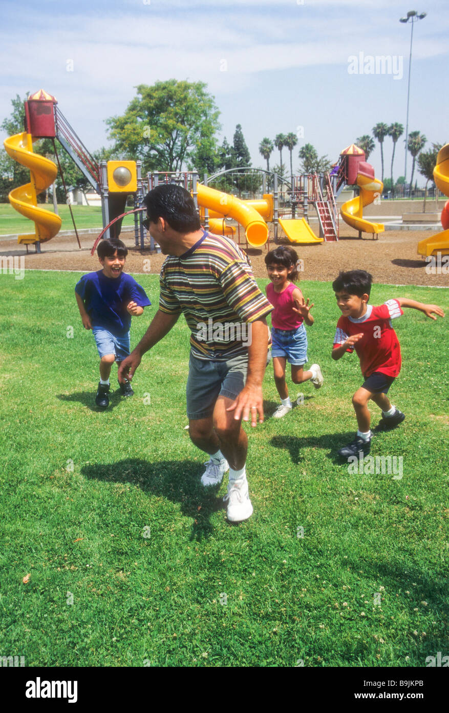 Hispanic father play tag with children boy girl son daughter kid run ...