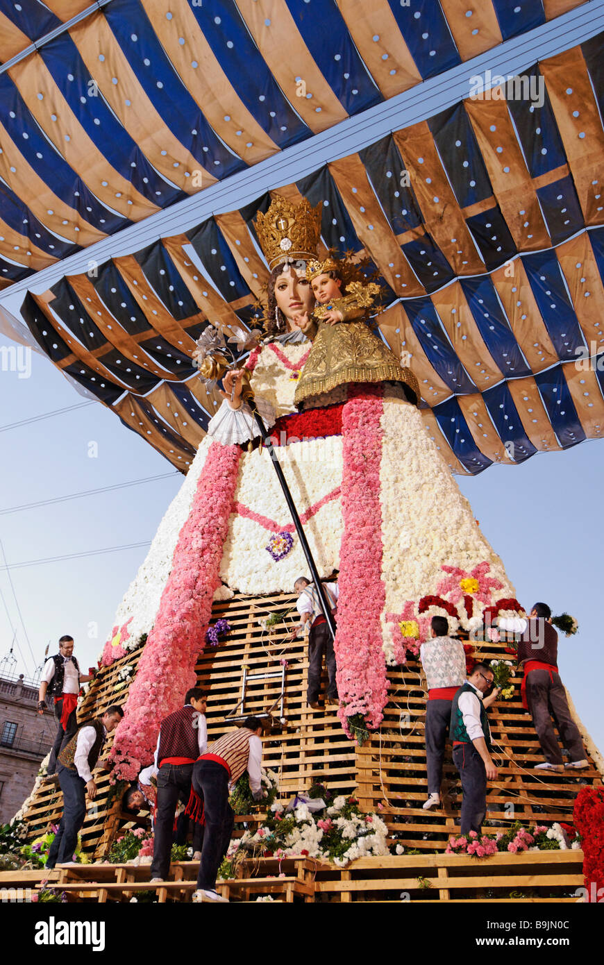 Men placing flower offerings on large wooden replica statue of Virgen ...