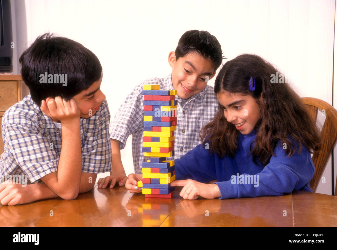 Three Hispanic kid boy girl brother sister twin play Jenga balance wood ...