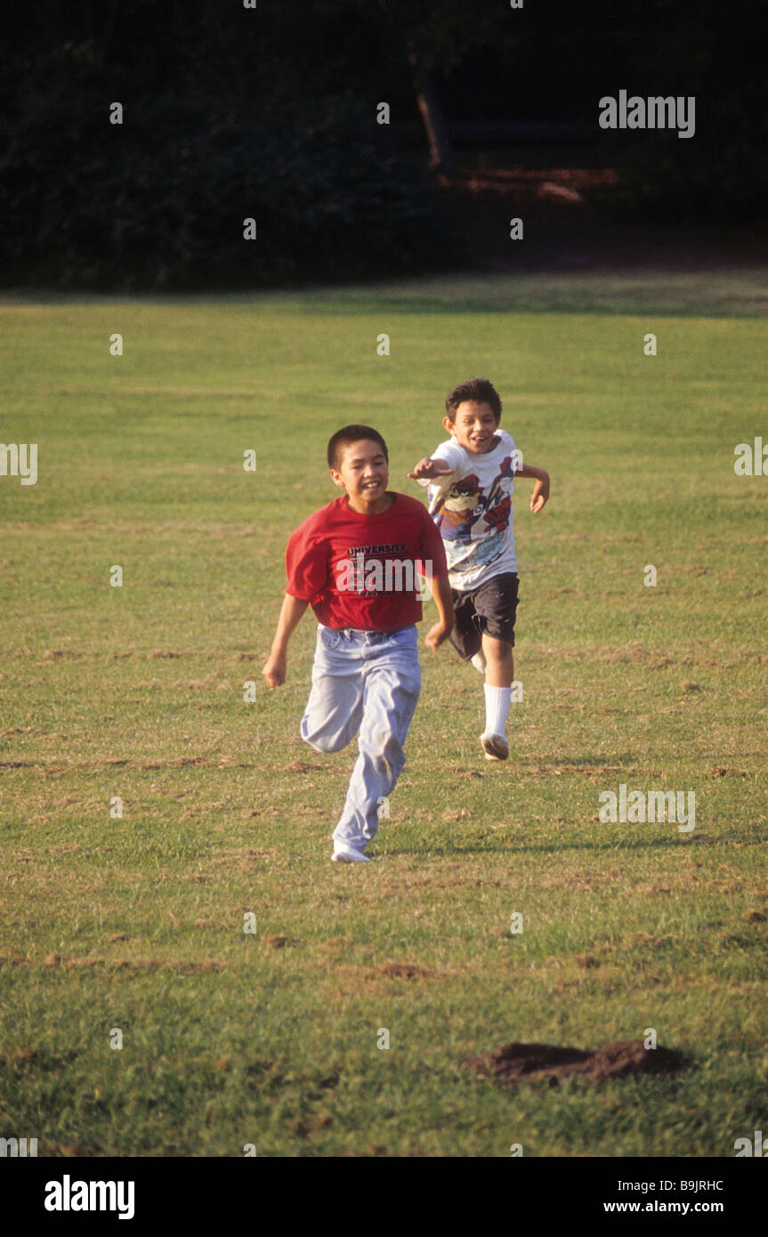 Two Hispanic boy chase tag run play park grass enjoy fun exercise sport ...