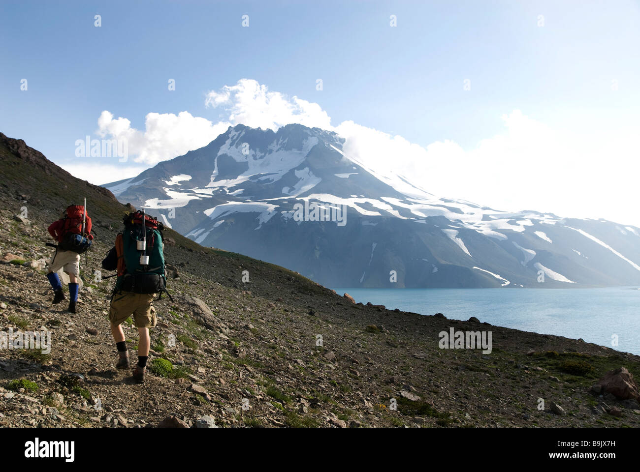 Two backpackers follow a trail around an alpine lake near the border of ...