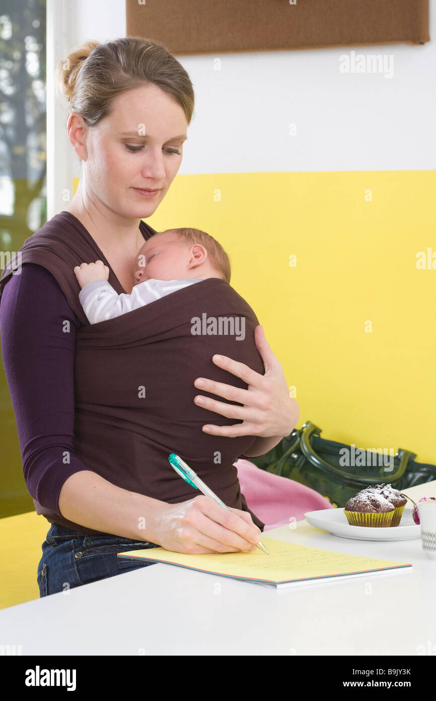 Mother with baby in baby sling, writing Stock Photo - Alamy