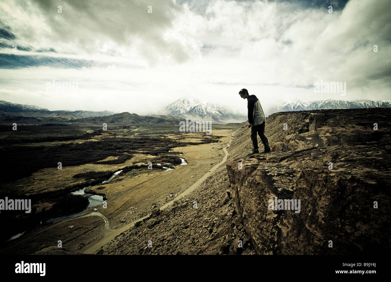 One man looks down the cliff face of a lava butte overlooking a grassy ...